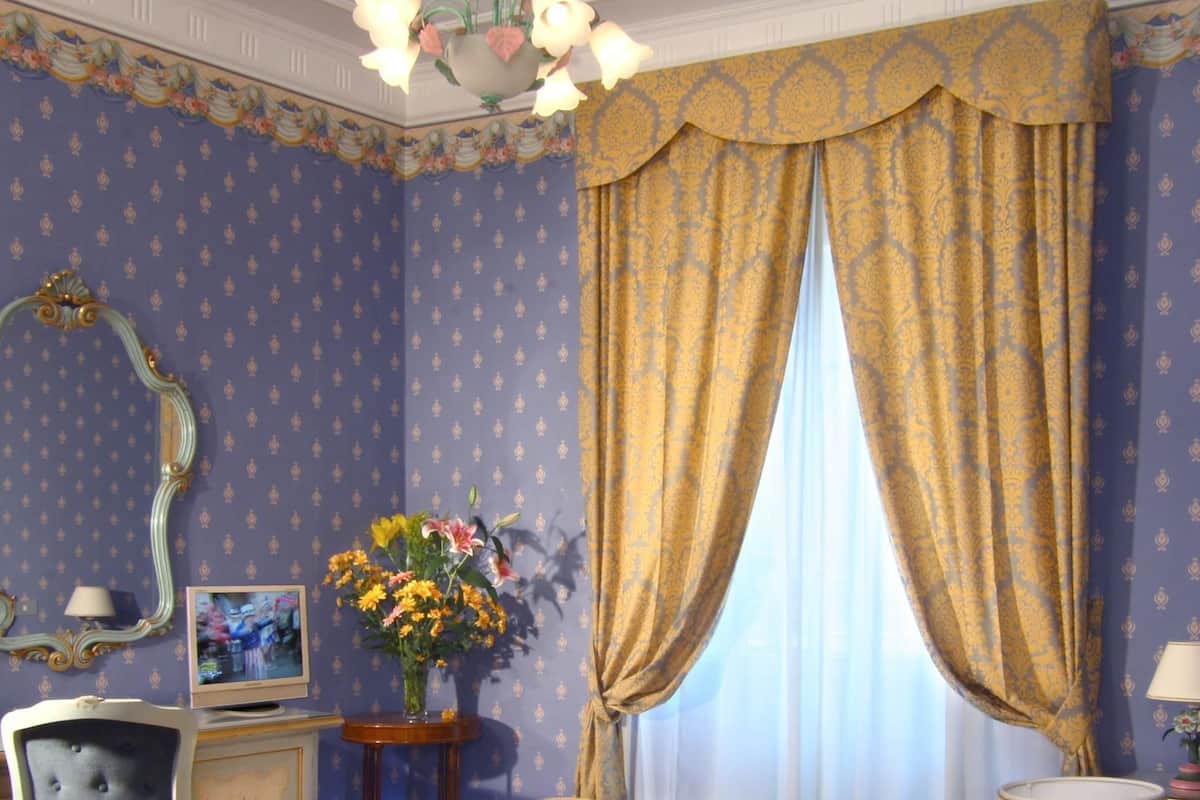 Quarto com cama, cômoda com abajur, cadeira, espelho e televisão sobre um suporte.
