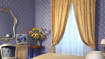 Quarto com cama, cômoda com abajur, cadeira, espelho e televisão sobre um suporte.