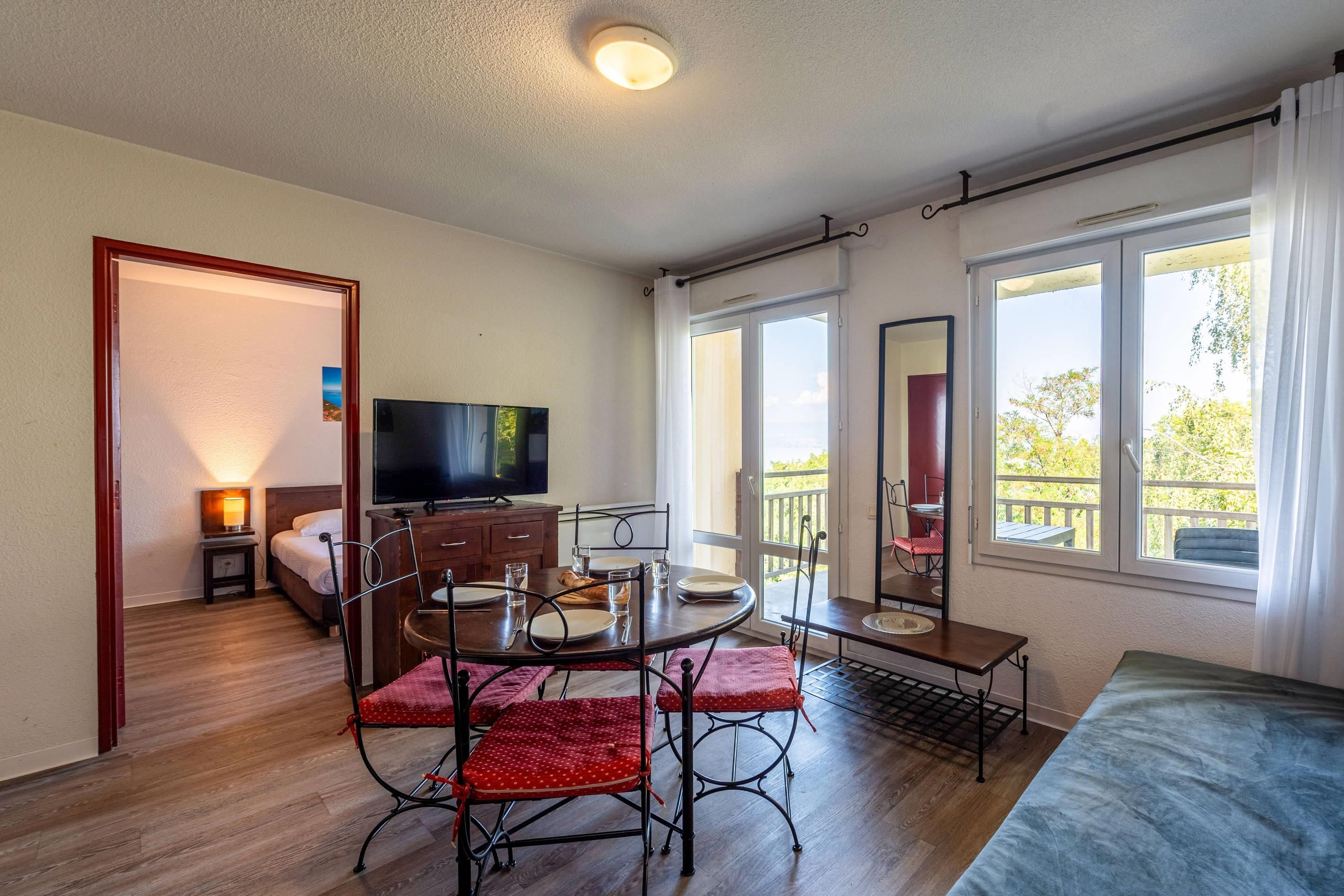 Quarto de hotel com área de jantar, cama, televisão e varanda com vista.