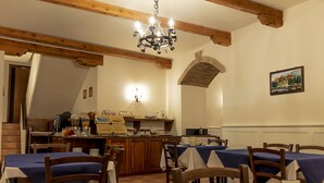 Uma sala de jantar com mesas cobertas por toalhas azuis, cadeiras de madeira e um candelabro.