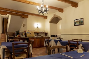 Uma sala de jantar com mesas cobertas por toalhas azuis, cadeiras de madeira e um candelabro.