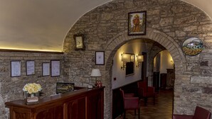 Um hall com um arco de pedra, uma mesa de recepção com um vaso de flores, certificados emoldurados e cadeiras vermelhas.