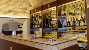 Uma área de bar com prateleiras cheias de garrafas de bebidas, copos e uma máquina de café.