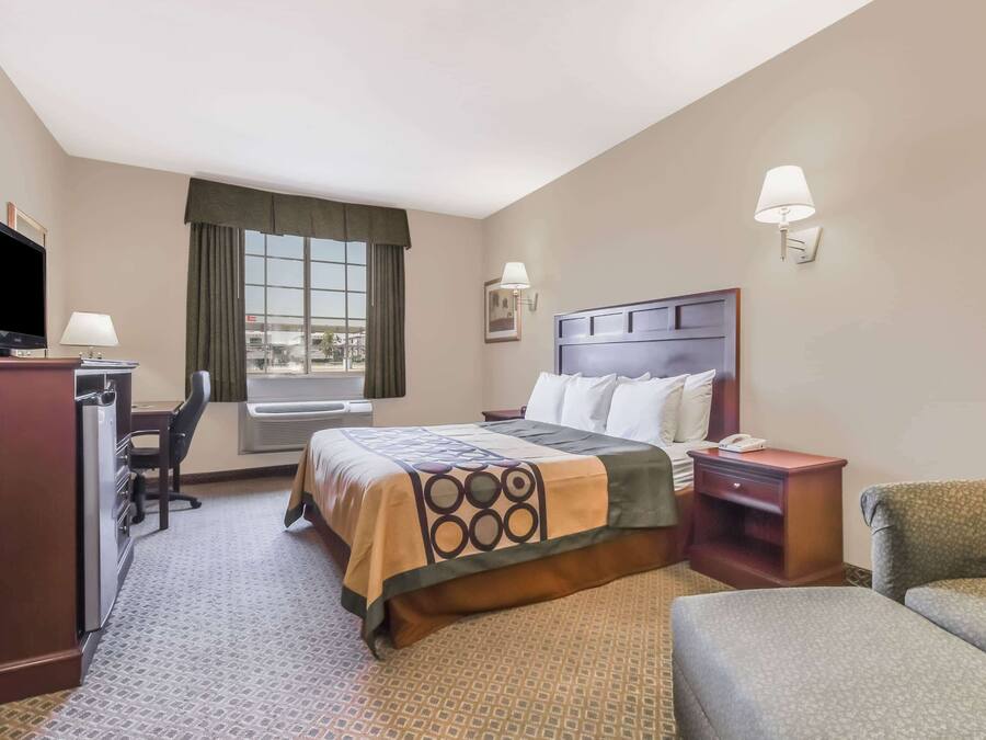 Quarto de hotel com cama, escrivaninha com computador, cadeira, televisão e janela com cortinas.