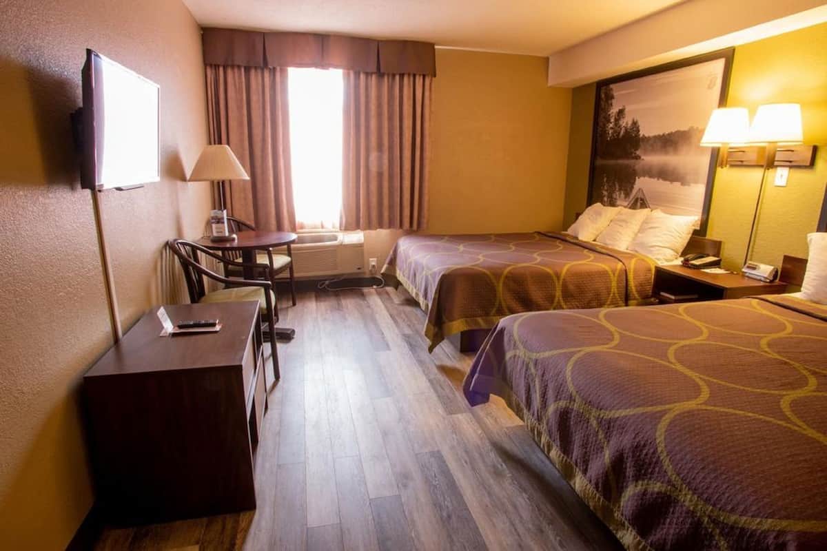 Quarto de hotel com duas camas, uma escrivaninha, uma cadeira, um abajur e um quadro na parede.