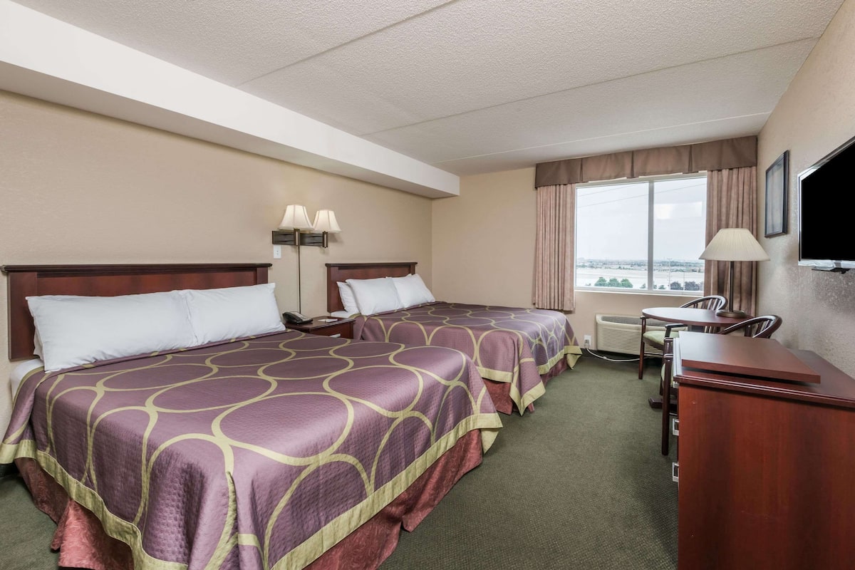 Quarto de hotel com duas camas, uma escrivaninha, uma cadeira, uma televisão e uma janela com vista.