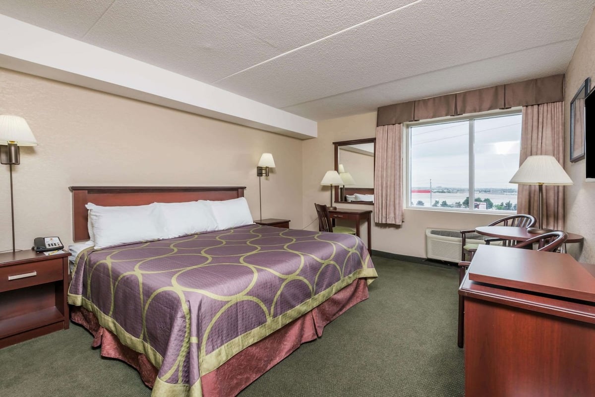 Quarto de hotel com uma cama grande, uma escrivaninha, uma cadeira, uma televisão e uma janela com vista.