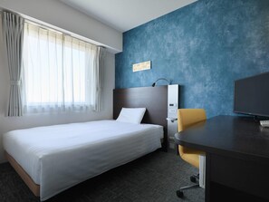 Quarto de hotel com cama, escrivaninha, cadeira, televisão e painel de controle fixado na parede.