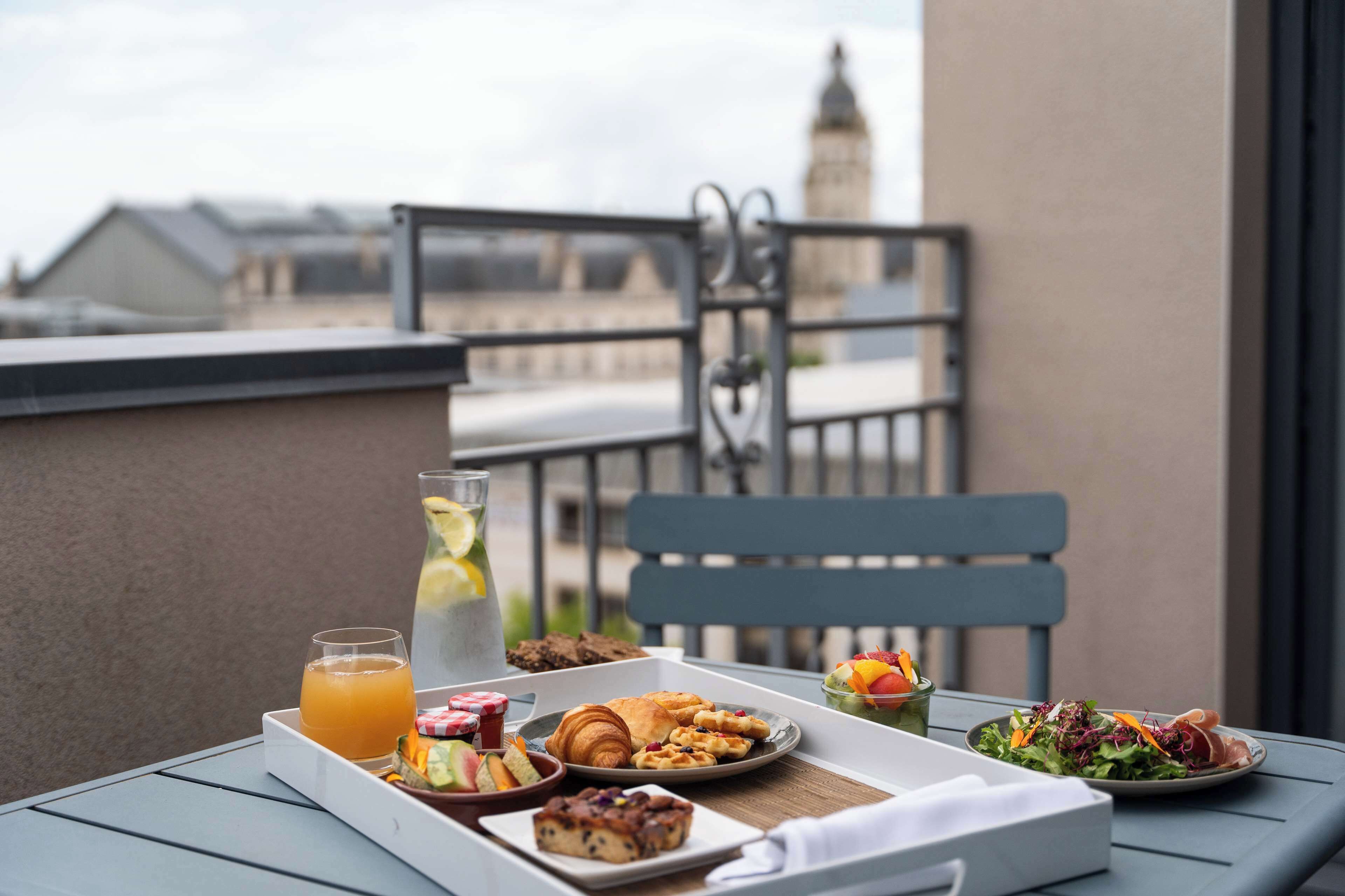Uma mesa na varanda com itens de café da manhã, incluindo croissants, muffins, salada de frutas e uma bebida.