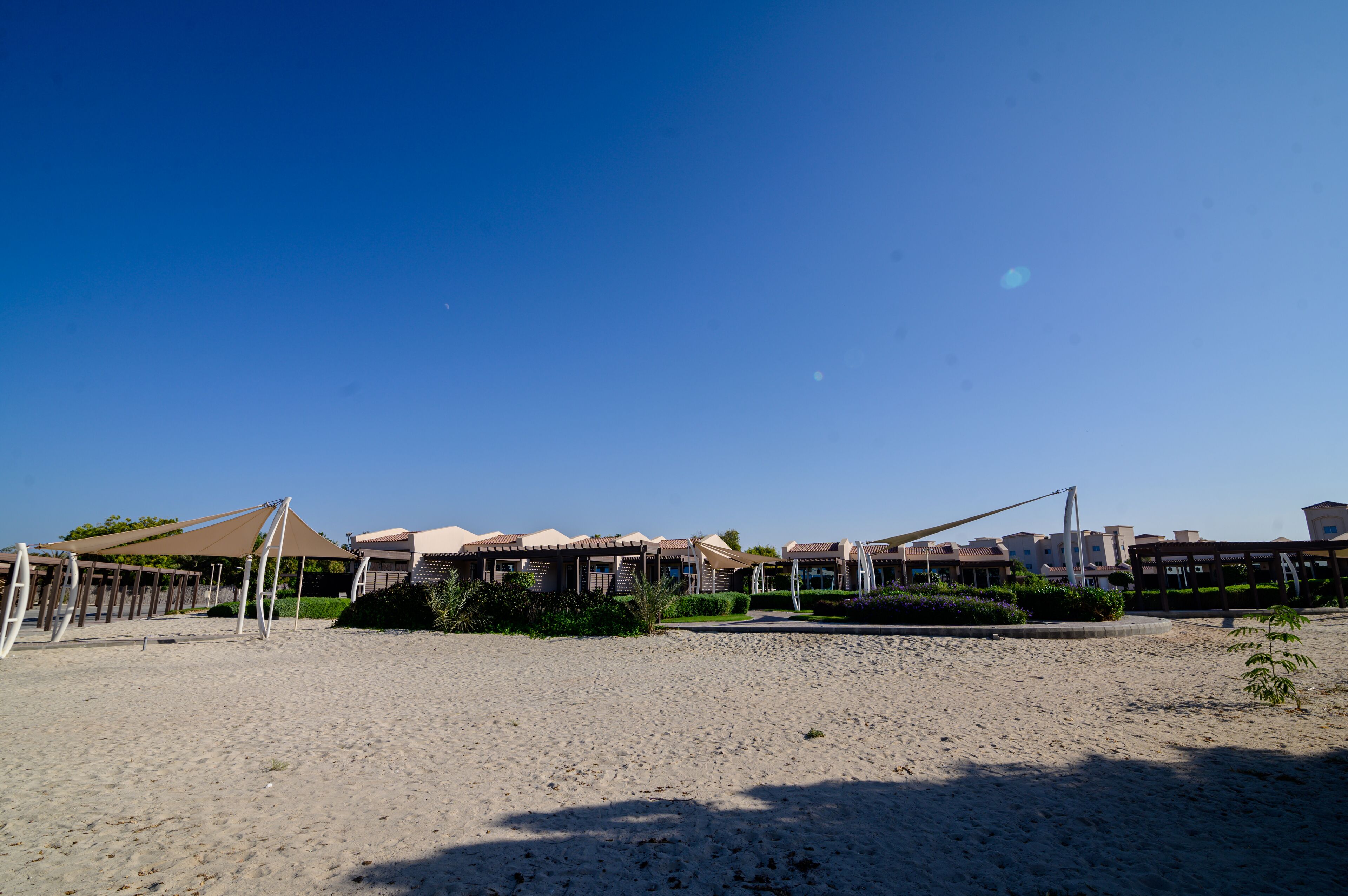 Uma área de praia arenosa com uma fileira de edifícios, incluindo um pavilhão coberto e uma construção com telhado branco.