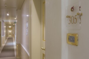 Corredor de hotel com uma porta identificada com o número '305' e um painel de controle digital na parede.