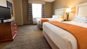 Quarto de hotel com duas camas, televisão, escrivaninha e janela com cortinas.