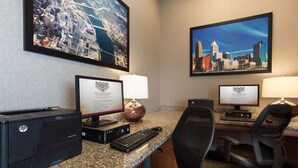 Quarto de hotel com dois computadores de mesa, uma impressora, um abajur e duas cadeiras de escritório.