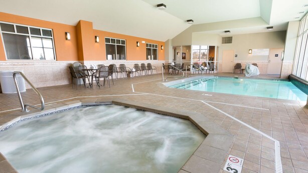 Uma área de piscina interna com hidromassagem, espreguiçadeiras e piso revestido de azulejos.