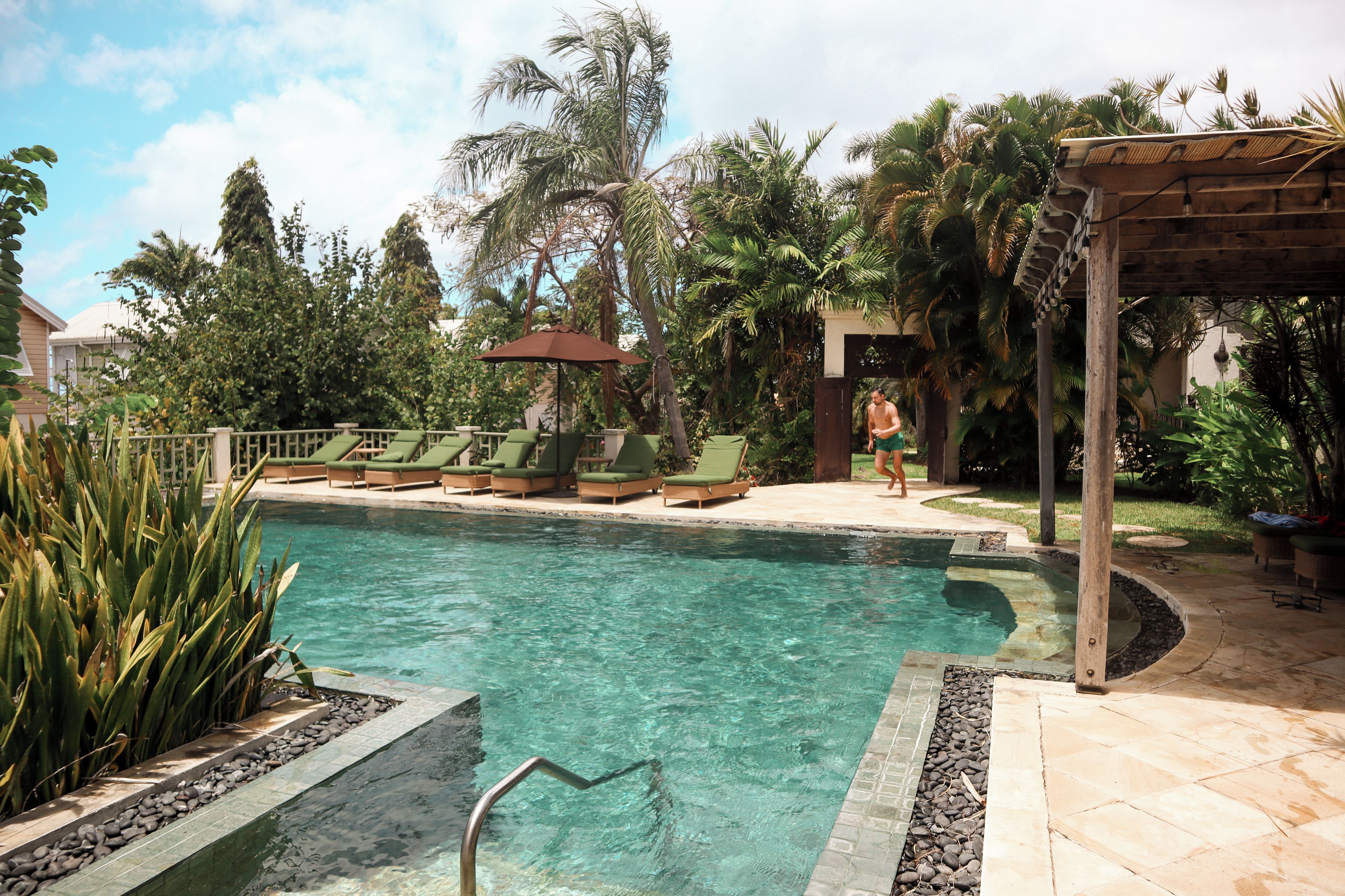 Área de piscina com espreguiçadeiras, pérgola e vegetação tropical.