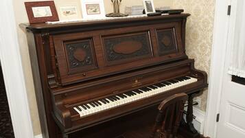 Um piano de cauda com acabamento em madeira e painéis decorativos, colocado numa sala com papel de parede estampado e uma porta branca.