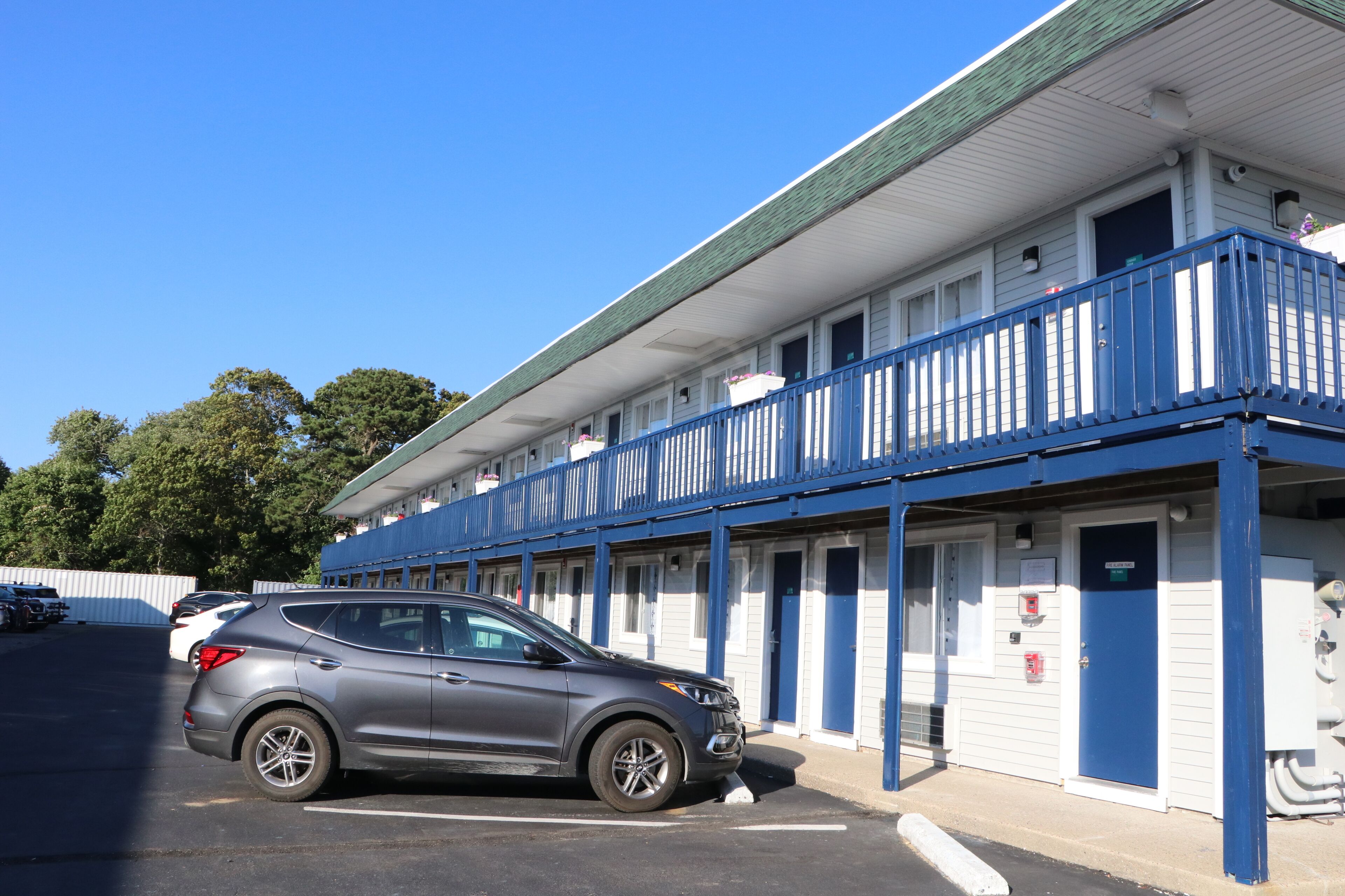 Um motel com uma fileira de quartos, cada um com uma varanda e uma porta numerada.