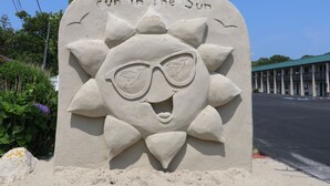Escultura de areia de um sol com óculos de sol e o texto 'Fun in the Sun' numa praia.