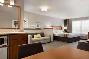 Quarto de hotel com cozinha compacta, cama, sofá, mesa de jantar e um espelho grande.