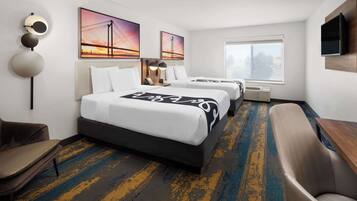 Quarto de hotel com duas camas, um sofá, uma TV e obras de arte nas paredes.