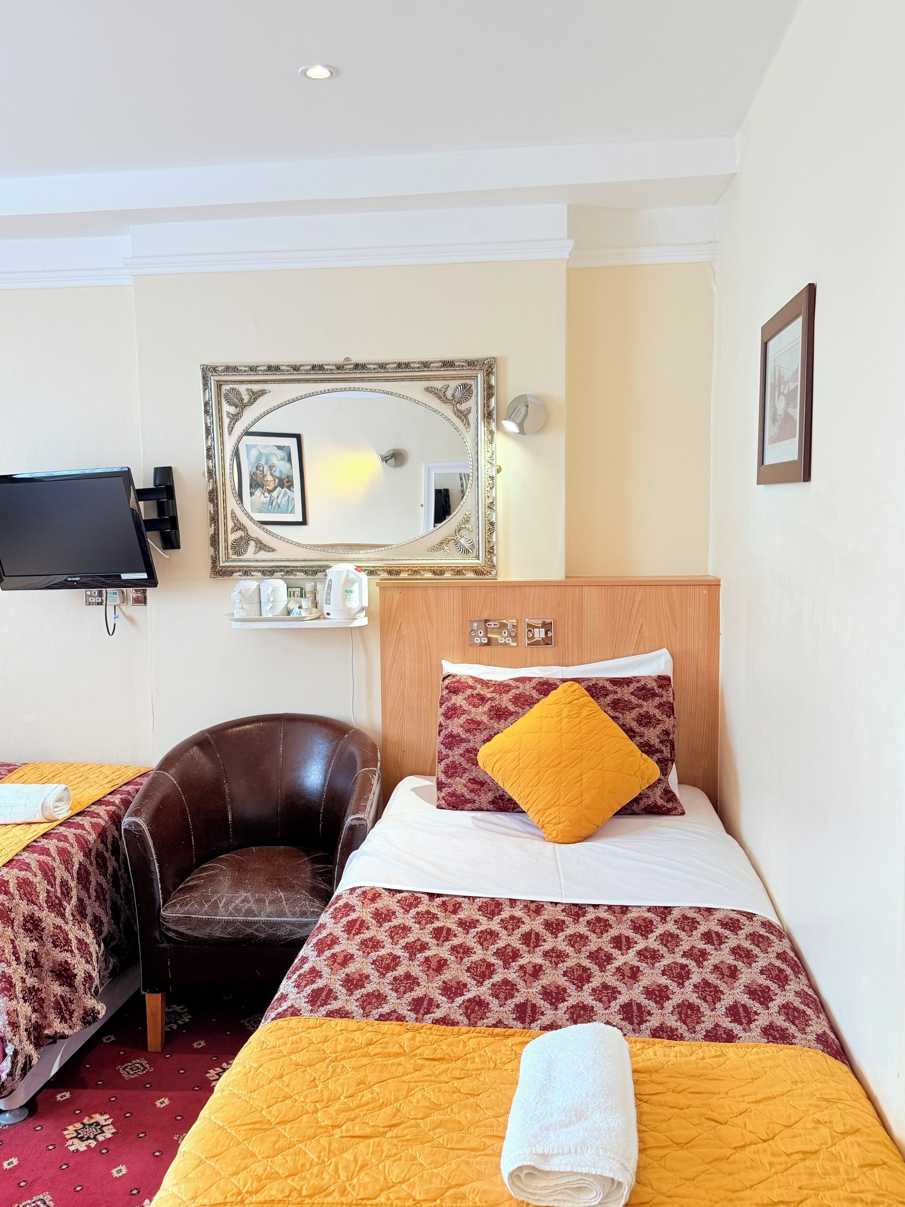 Quarto de hotel com uma cama, uma cadeira, uma televisão, um espelho e uma prateleira com produtos de higiene pessoal.