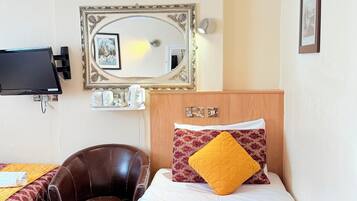 Quarto de hotel com uma cama, uma cadeira, uma televisão, um espelho e uma prateleira com produtos de higiene pessoal.