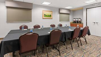 Sala de conferência com uma mesa comprida, cadeiras, garrafas de água e um canto para café.