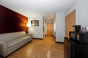 Quarto de hotel com sofá, micro-ondas, cafeteira e quadro emoldurado na parede.