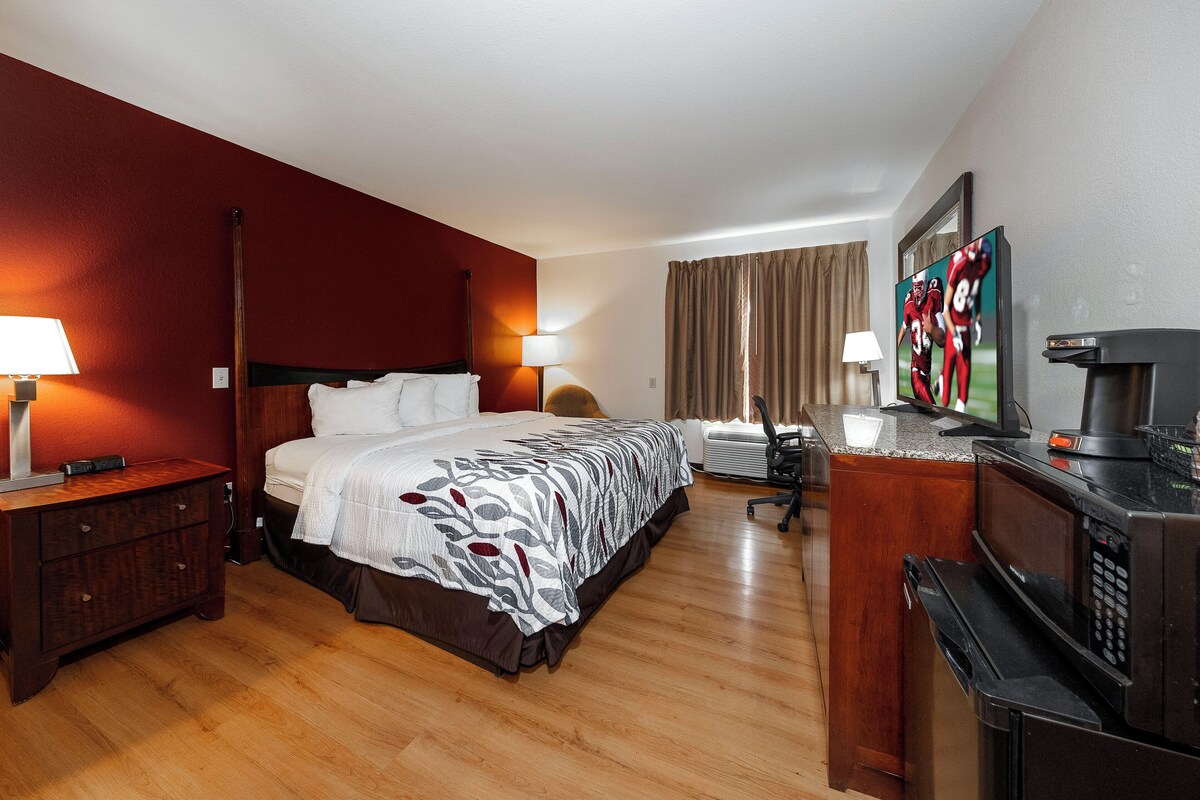 Quarto de hotel com cama, escrivaninha, cadeira, televisão e micro-ondas.