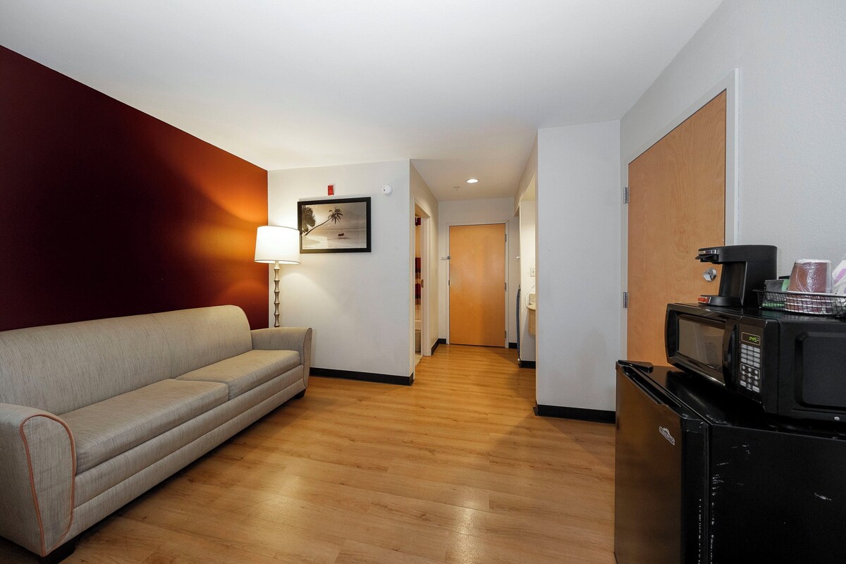 Quarto de hotel com sofá, micro-ondas, cafeteira e quadro na parede.