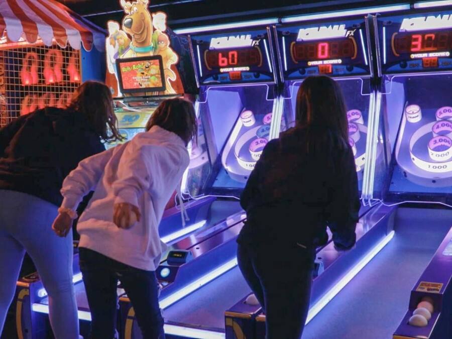 Um grupo de pessoas jogando em uma máquina de peguinha em um fliperama.
