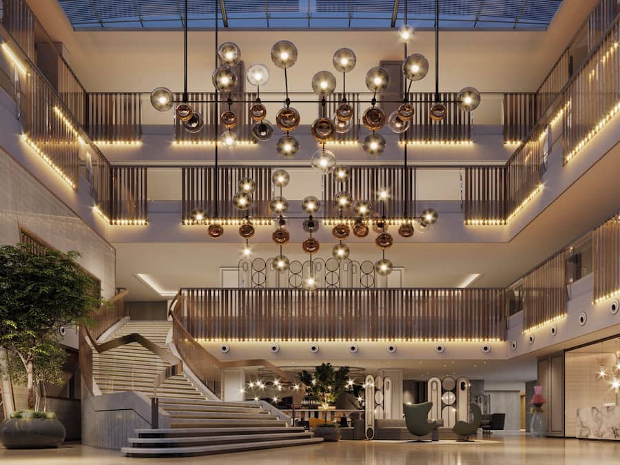 Um hall espaçoso com uma escadaria imponente, lustres modernos e um balcão de recepção.