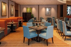 Um restaurante com mesas redondas, cadeiras azuis e bancos laranja.