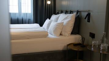 Quarto de hotel com duas camas, uma mesinha de cabeceira com um controle remoto e uma pequena mesa com dois copos.