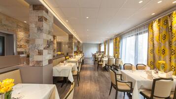 Um restaurante com várias mesas, pilares de pedra e cortinas estampadas em amarelo.