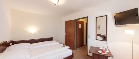 Quarto de hotel com cama, mesa de cabeceira, televisão e espelho.