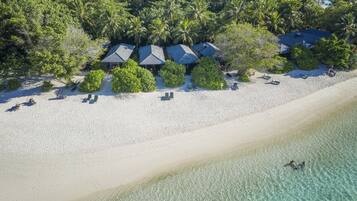 Vista aérea de um resort à beira-mar com várias construções em estilo de bangalô, cercadas por vegetação tropical densa.