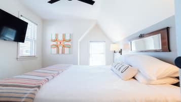 Quarto com cama, ventoinha no teto, televisão, janela e uma obra de arte na parede.