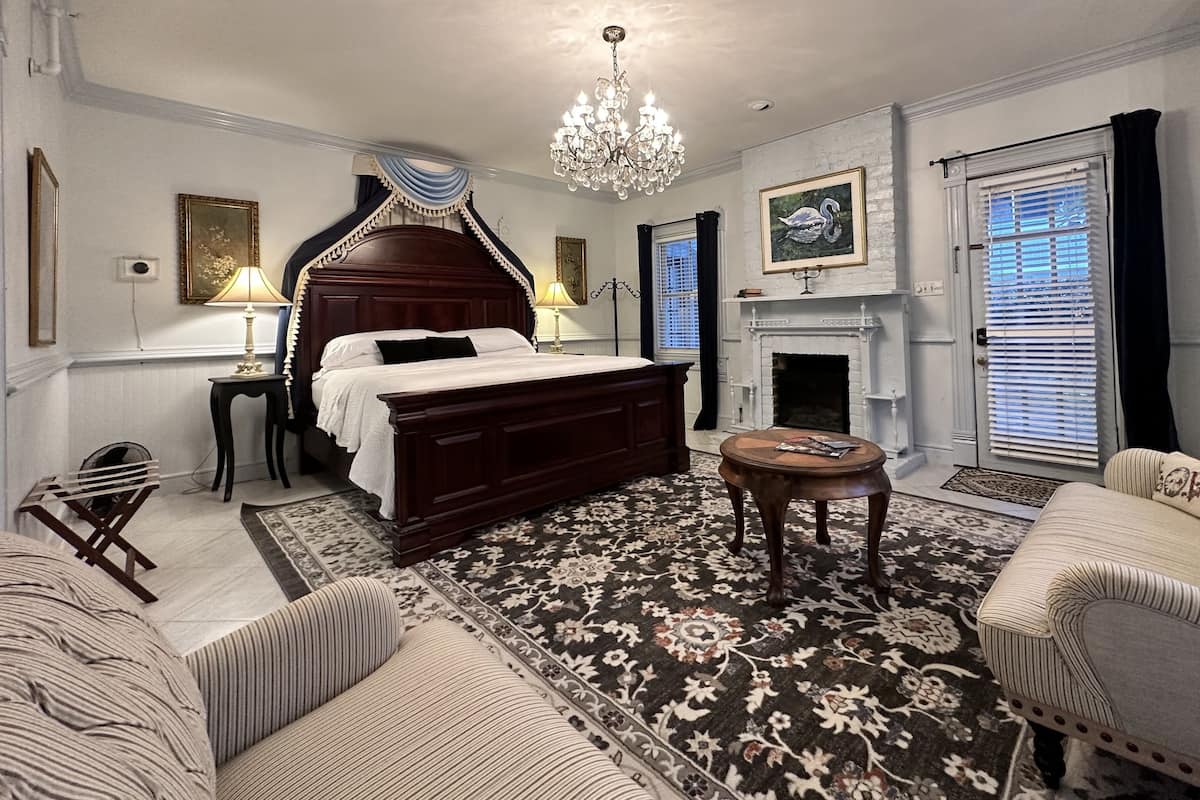 Um quarto clássico com uma cama de dossel, um candelabro, uma lareira e uma poltrona listrada.