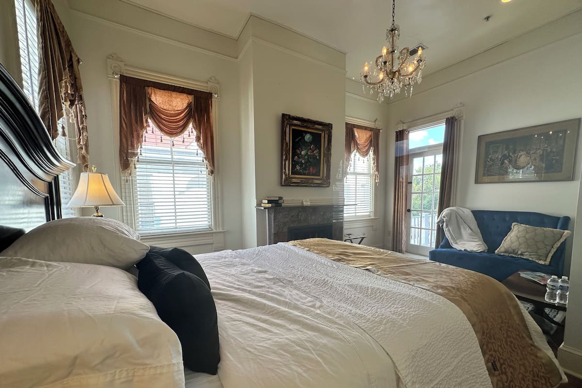 Quarto de hotel com uma cama grande, um sofá azul, um candelabro e uma lareira.
