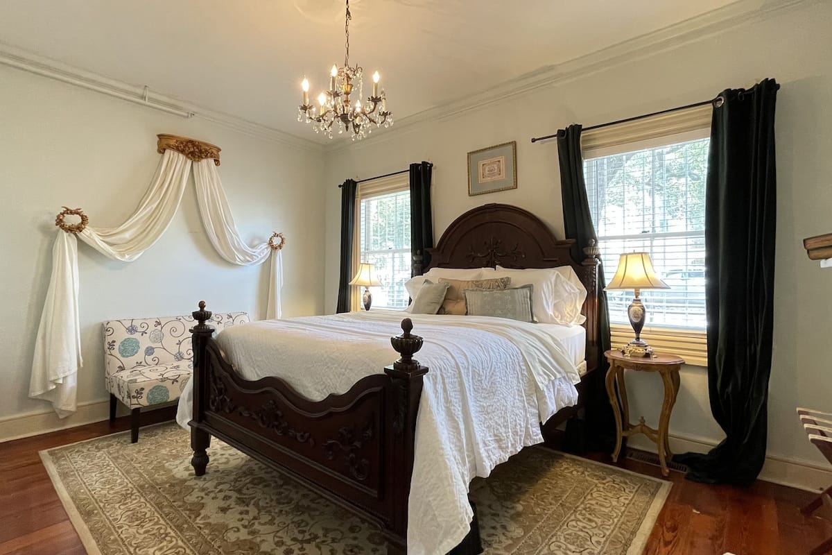 Quarto tradicional com cama de dossel, um candelabro e uma janela grande com cortinas.