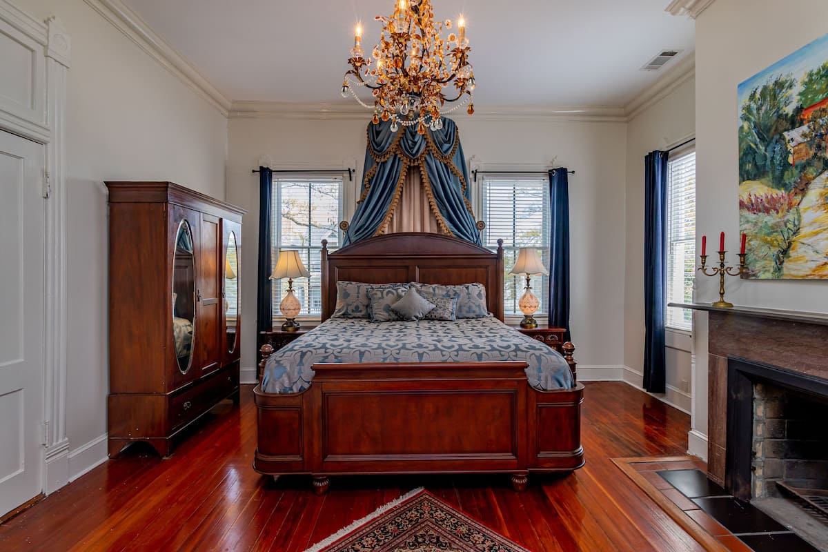 Um quarto espaçoso com uma cama grande, um candelabro, uma lareira e um quadro na parede.