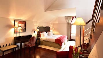 Quarto de hotel com cama, mesas de cabeceira, escrivaninha, cadeira e luminária.