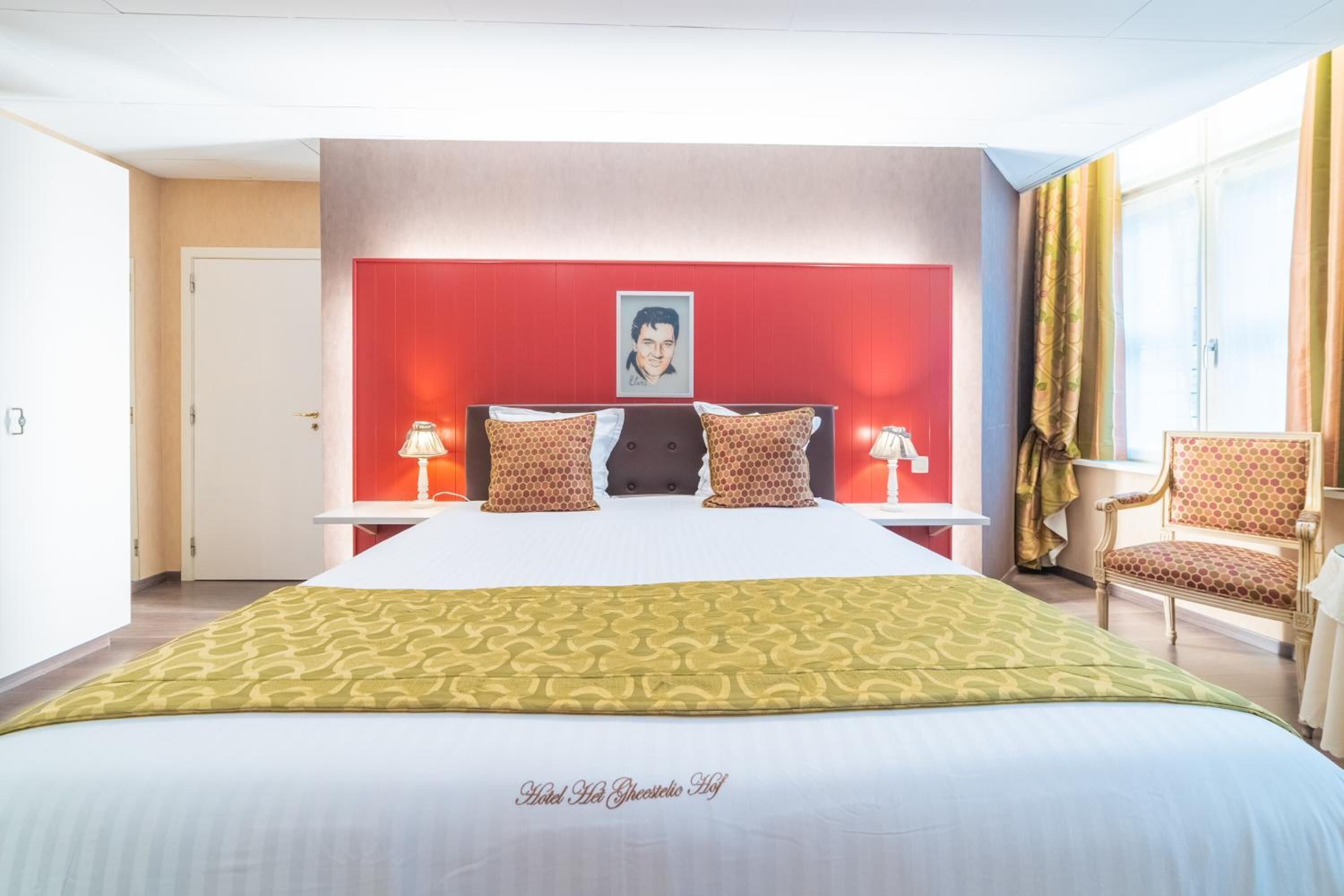 Quarto de hotel com uma cama grande, duas mesas de cabeceira com luminárias, uma parede com detalhes em vermelho e um quadro acima da cama.