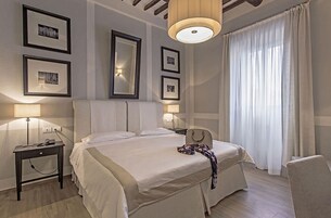 Quarto de hotel bem organizado, com uma cama grande, abajures, um espelho e quadros nas paredes.