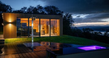 Uma casa moderna com grandes janelas de vidro, um deck de madeira e uma banheira de hidromassagem.