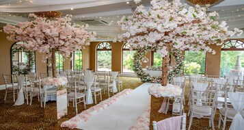 Espaço para casamentos com cadeiras brancas, um corredor branco e grandes arranjos florais.
