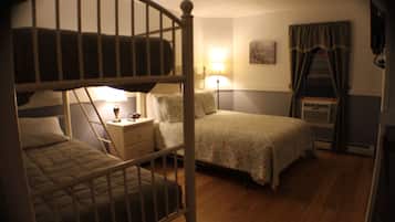 Quarto com beliches, mesa de cabeceira com abajur, cômoda, janela com cortinas e TV fixada na parede.