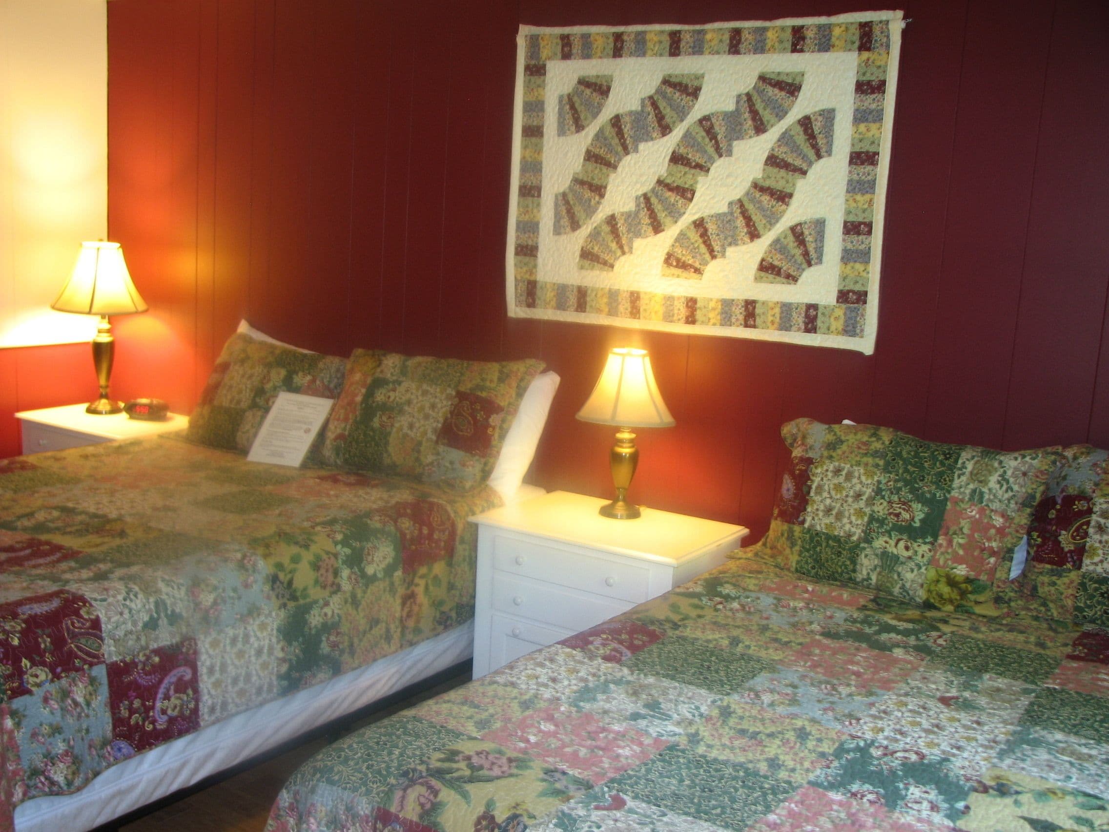 Uma cama de casal com roupa de cama floral, duas luminárias de cabeceira, uma mesinha de cabeceira branca e um painel de parede acolchoado.