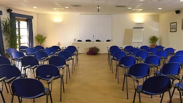 Uma sala de conferências com fileiras de cadeiras azuis, um quadro branco e um pódio com microfones.